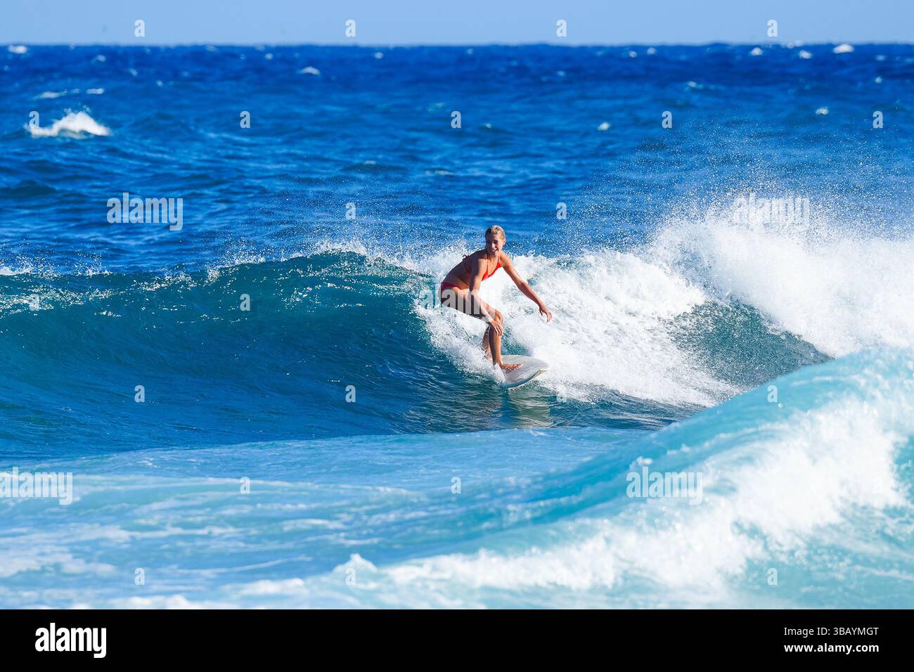Surfer rides a powerful wave in tropical blue waters wearing a red ...