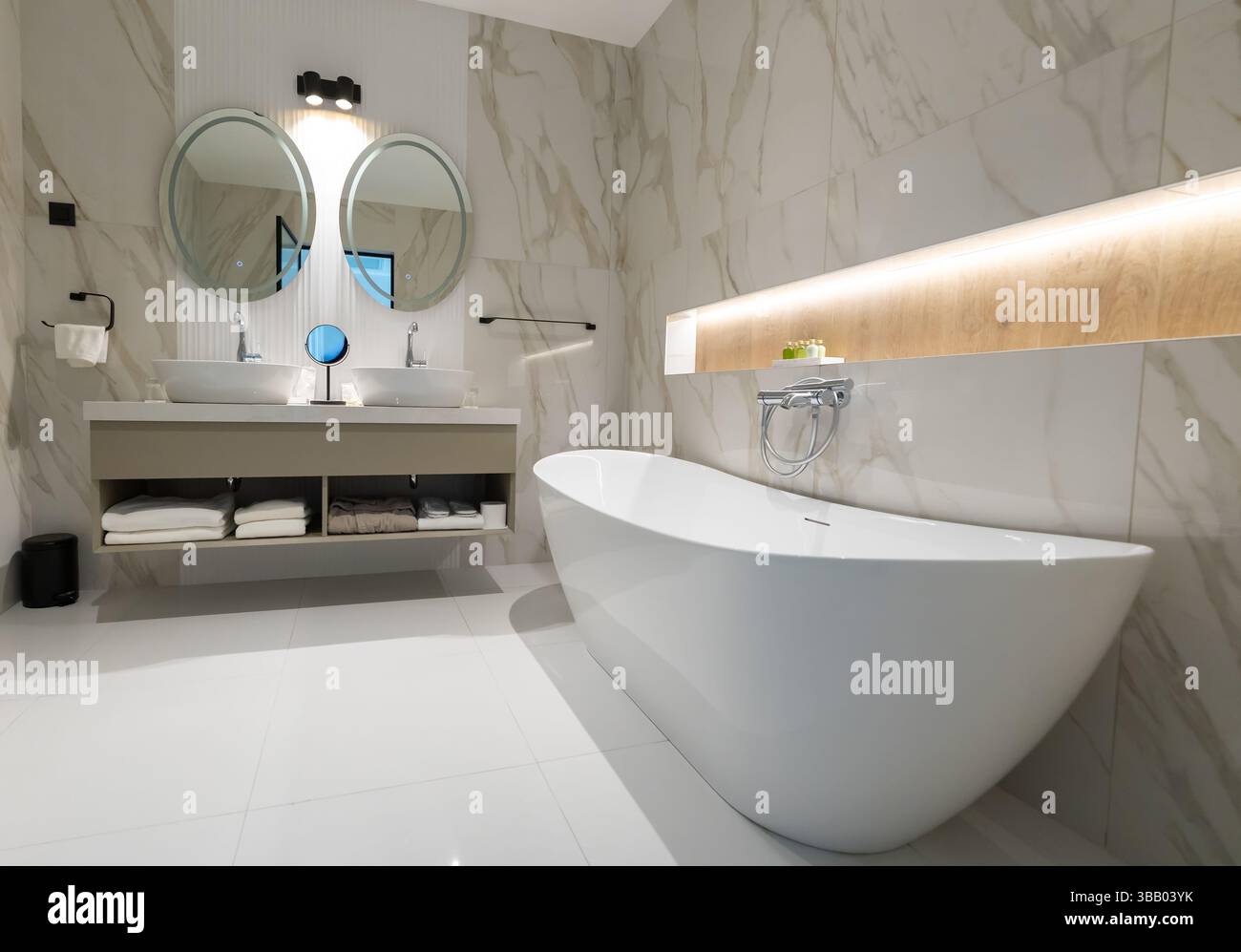 A modern elegant hotel bathroom with freestanding tub, double sink and ...
