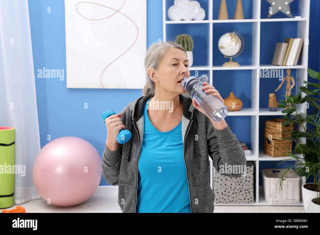 Elderly woman drinking water during exercise with dumbbell at home ...