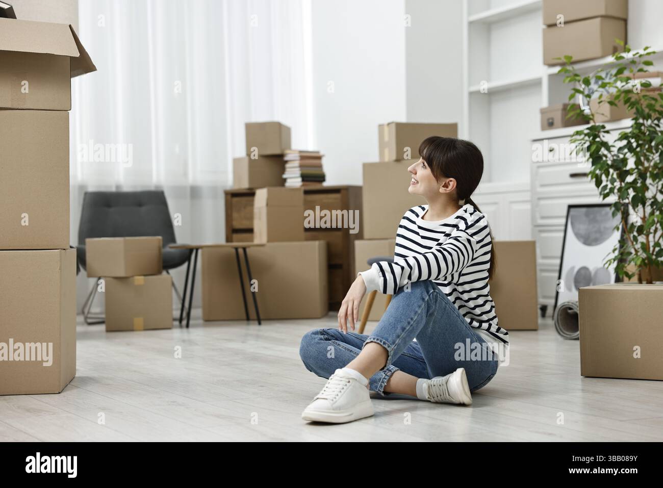 Moving day. Happy woman resting on floor and cardboard boxes in her new ...
