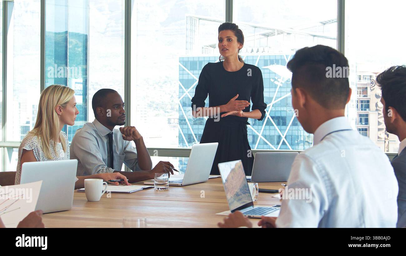 Businesswoman Giving Presentation To Business Team Sitting Around Table ...