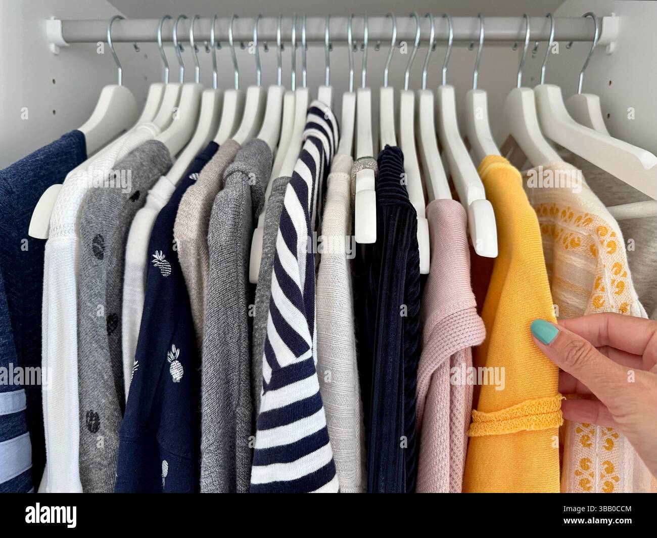 Close-up of a woman's hand picking which top to wear from a selection ...