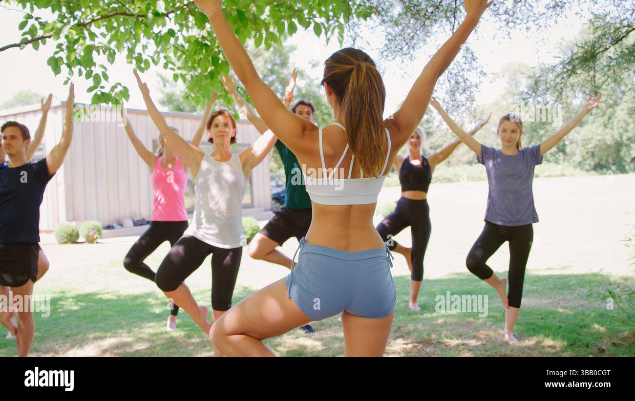 Female Instructor Leading Group Of People In Outdoor Yoga Class Stock ...