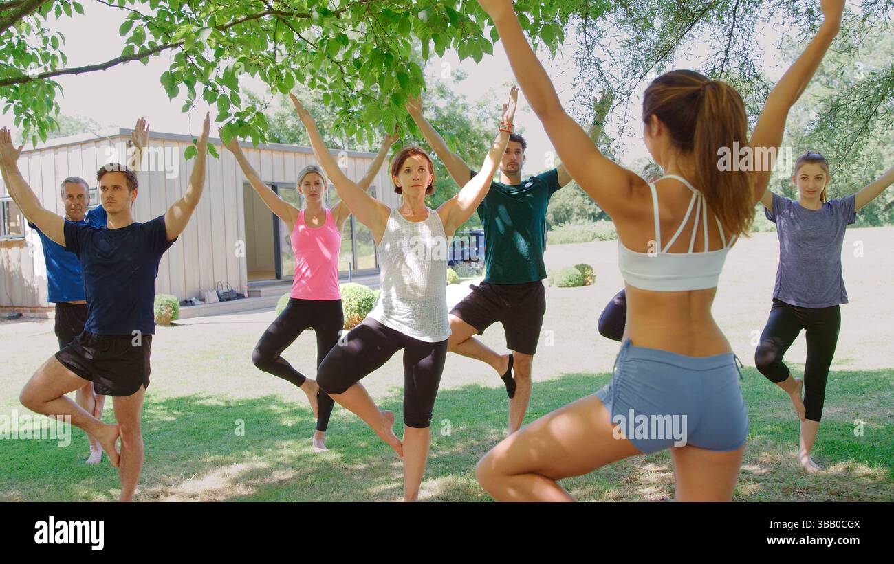 Female Instructor Leading Group Of People In Outdoor Yoga Class Stock ...