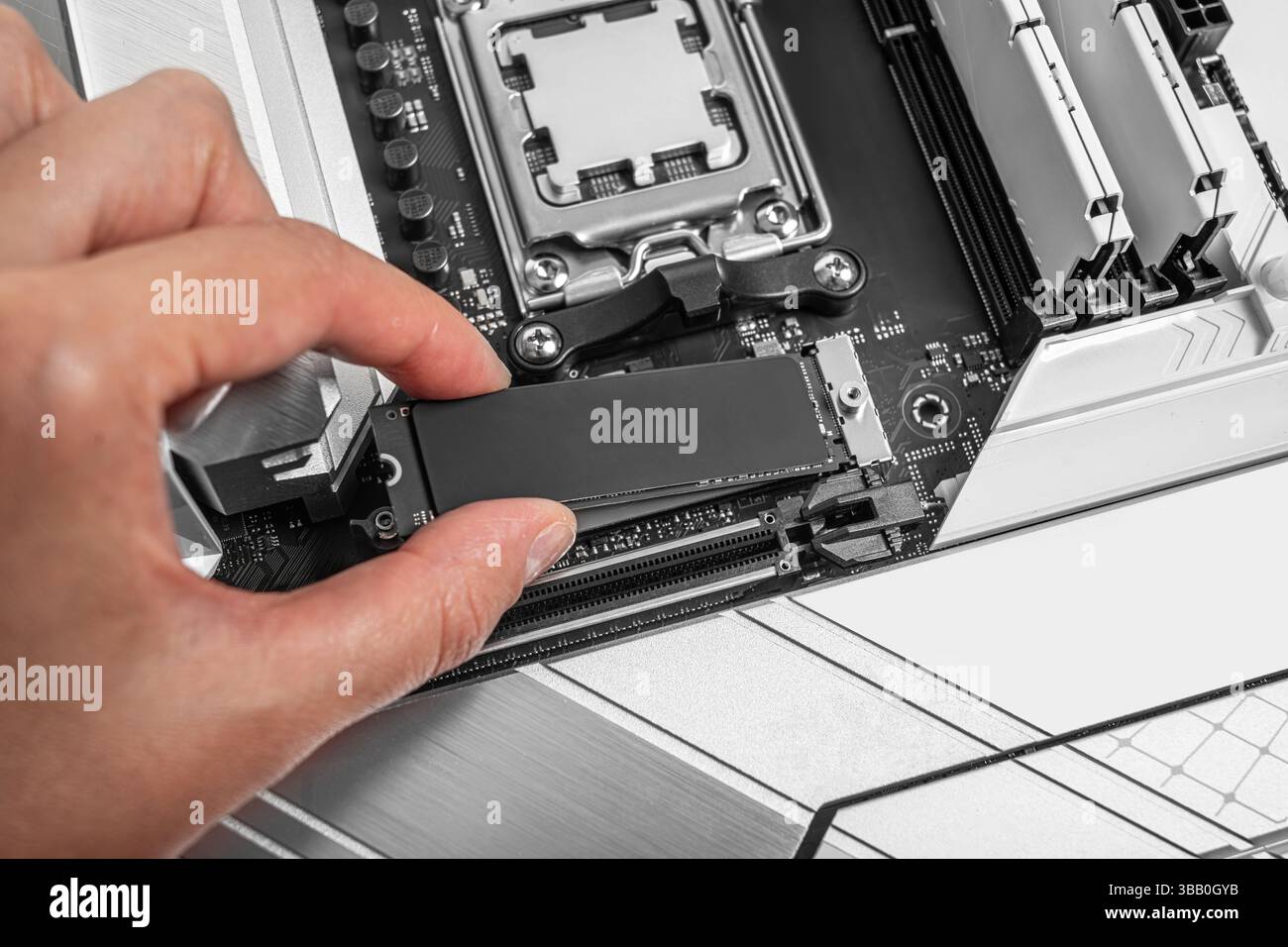 A person is installing an M.2 NVMe SSD into a modern motherboard socket ...