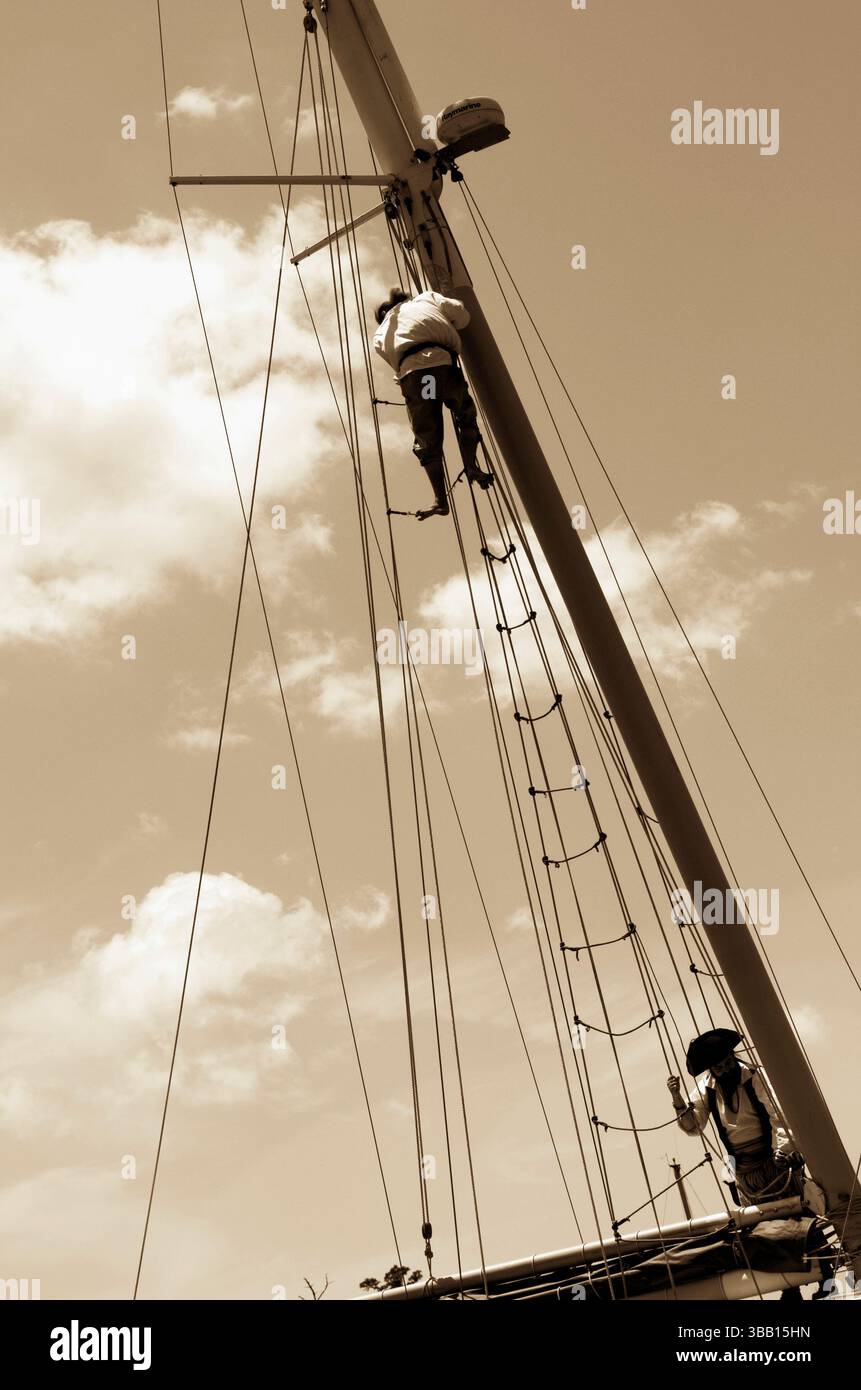 Man climbing the mast of a tall ship docked along the riverfront in ...
