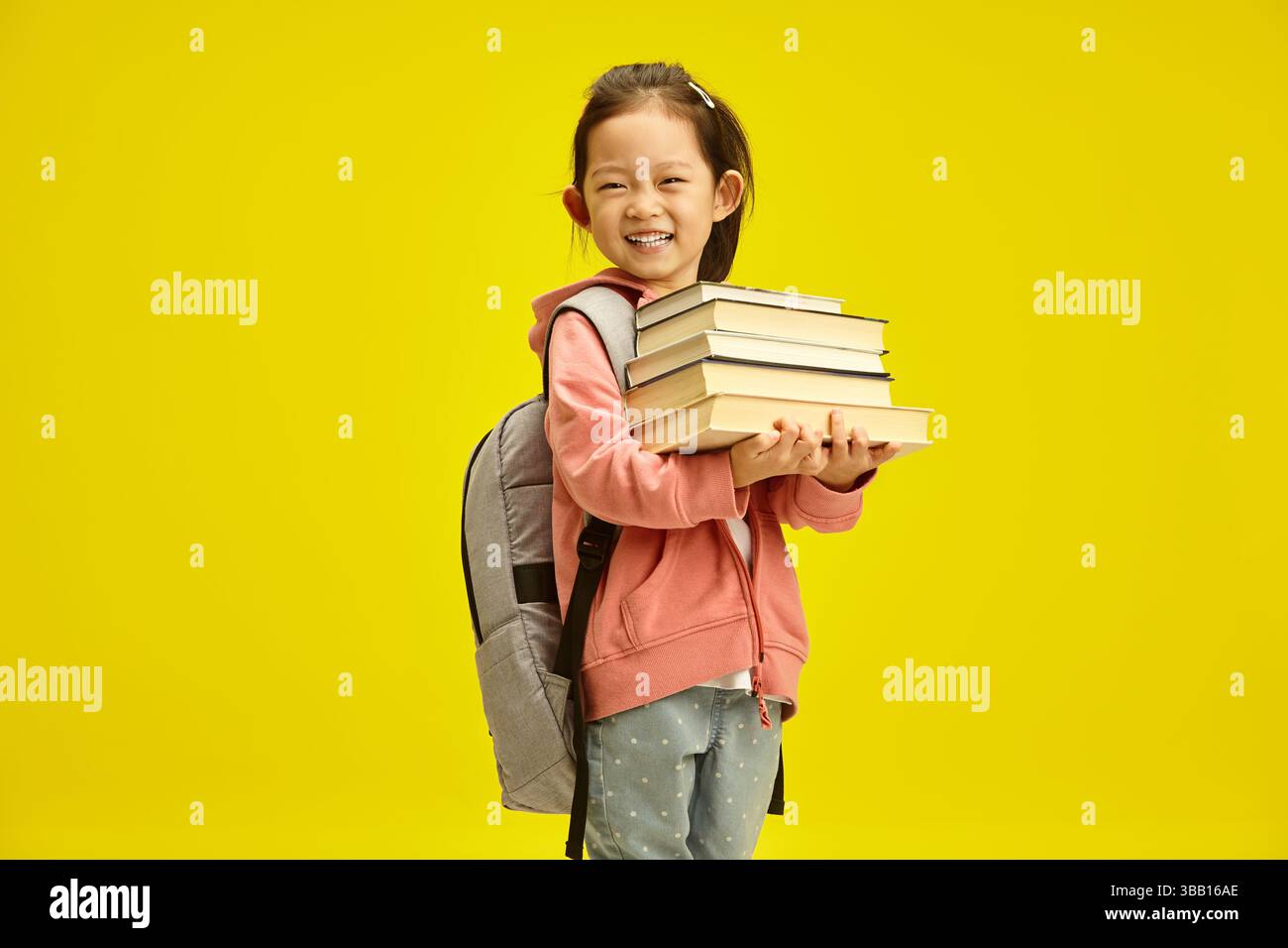 Happy chinese girl preparing going to the first grade, holds many different books in her hands ...