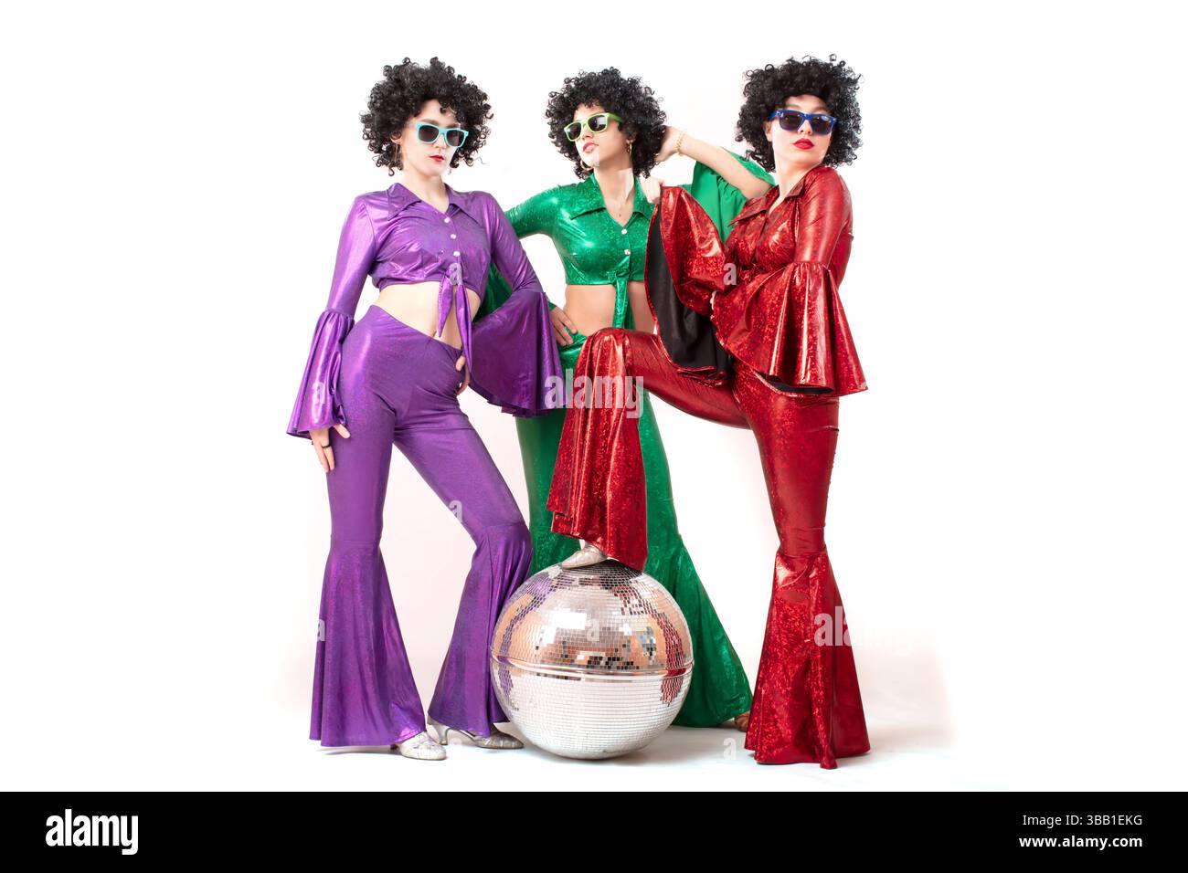 Three female pop stars in neon clothes pose in front of a silver ball ...