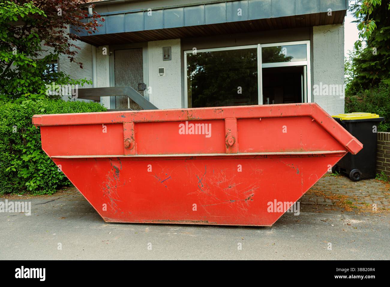 A bright red dumpster is positioned in front of a house, ready for ...