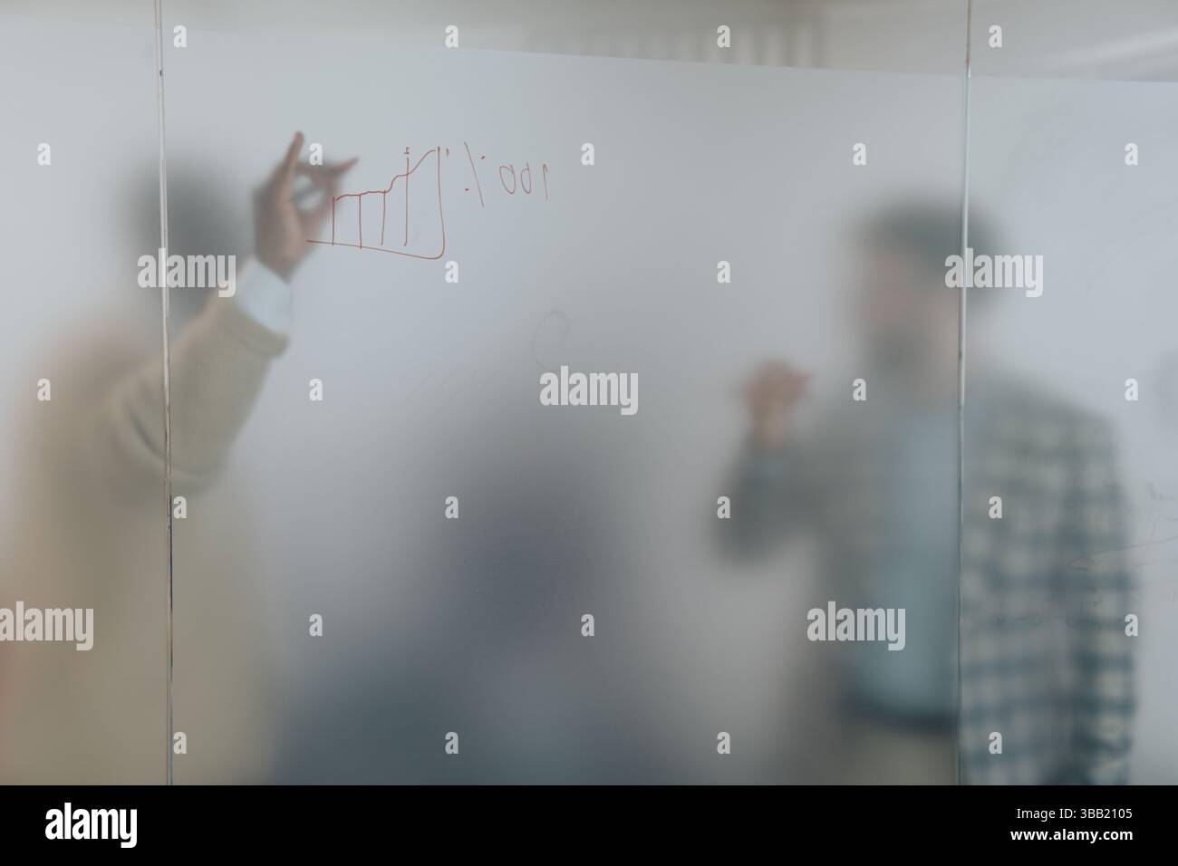 A group of colleagues are brainstorming, drawing charts on a frosted ...