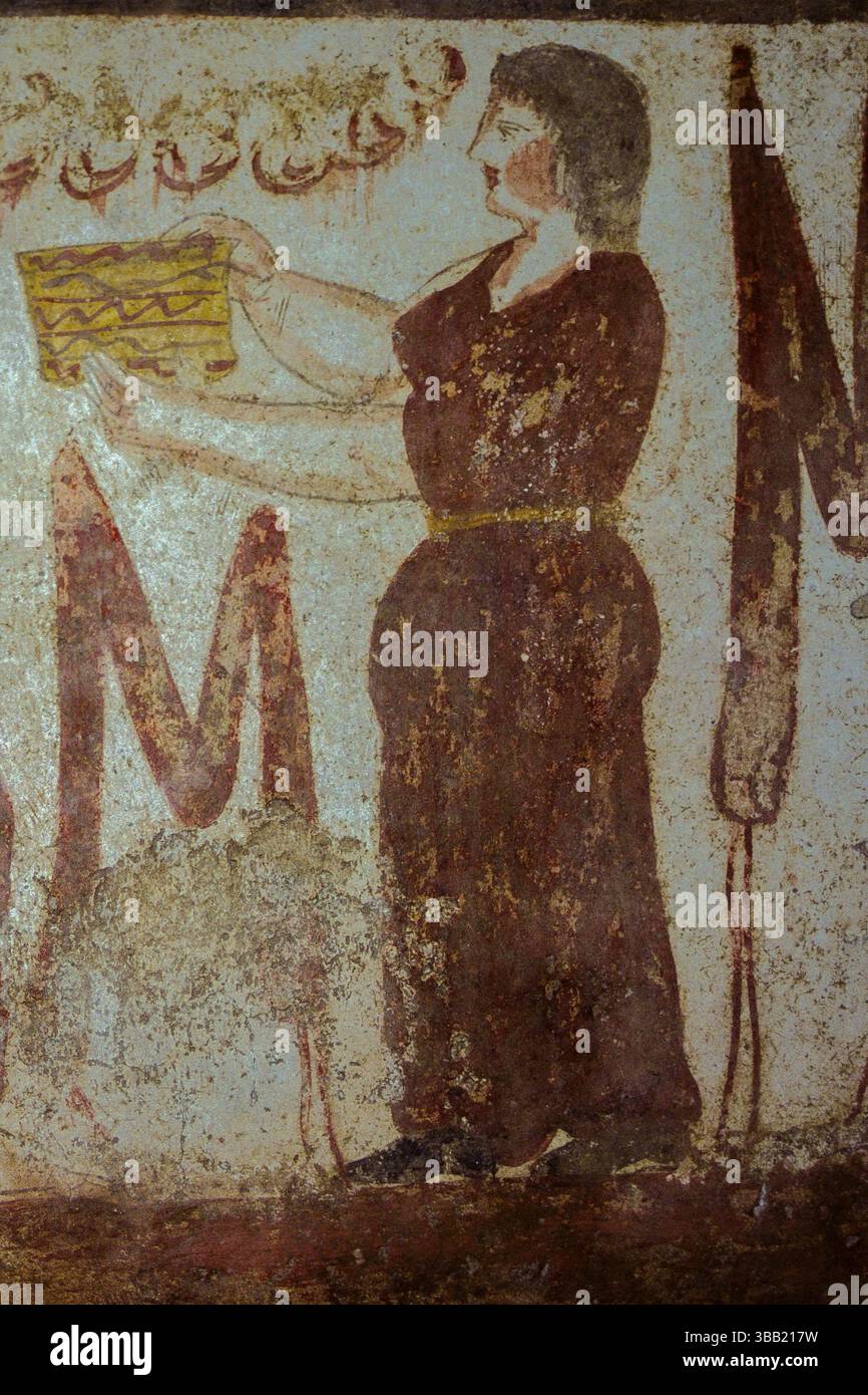 Female mourner wearing long red gown holds basket under pomegranates ...