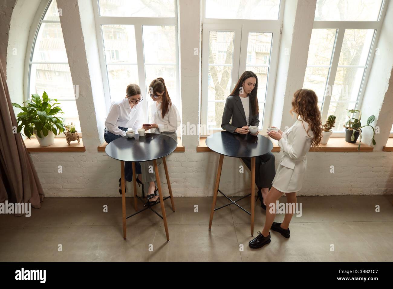 Colleagues gather near high tables in modern office during break, some ...