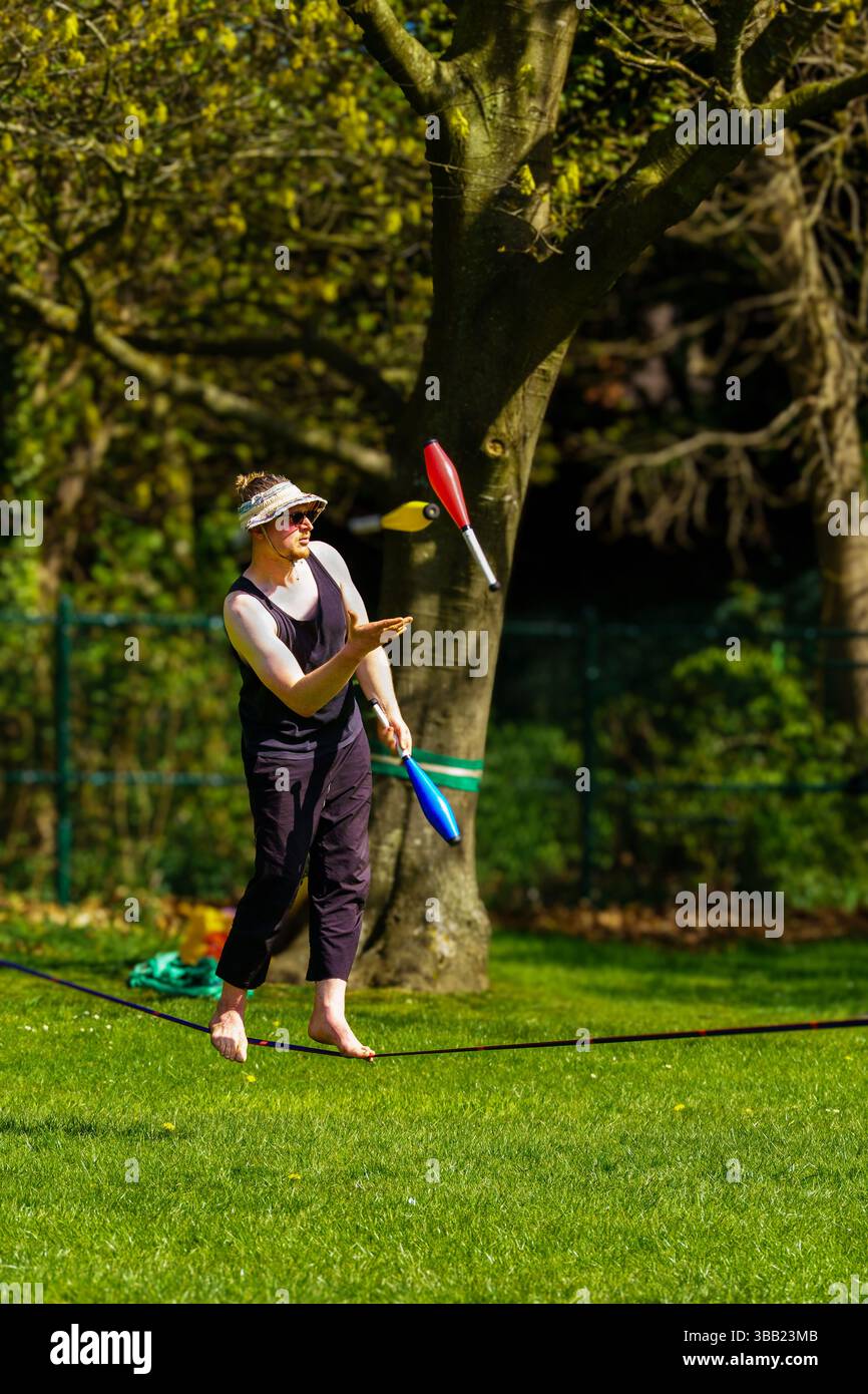 Outdoor street performer practises juggling and slacklining barefoot ...