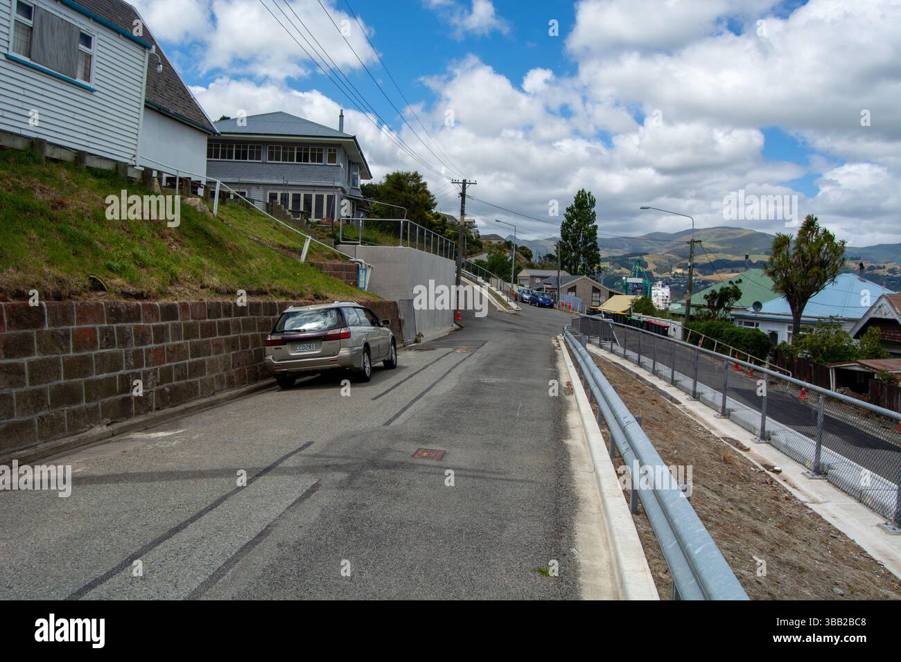 A quiet residential street with a sloped road, lined with houses and a ...