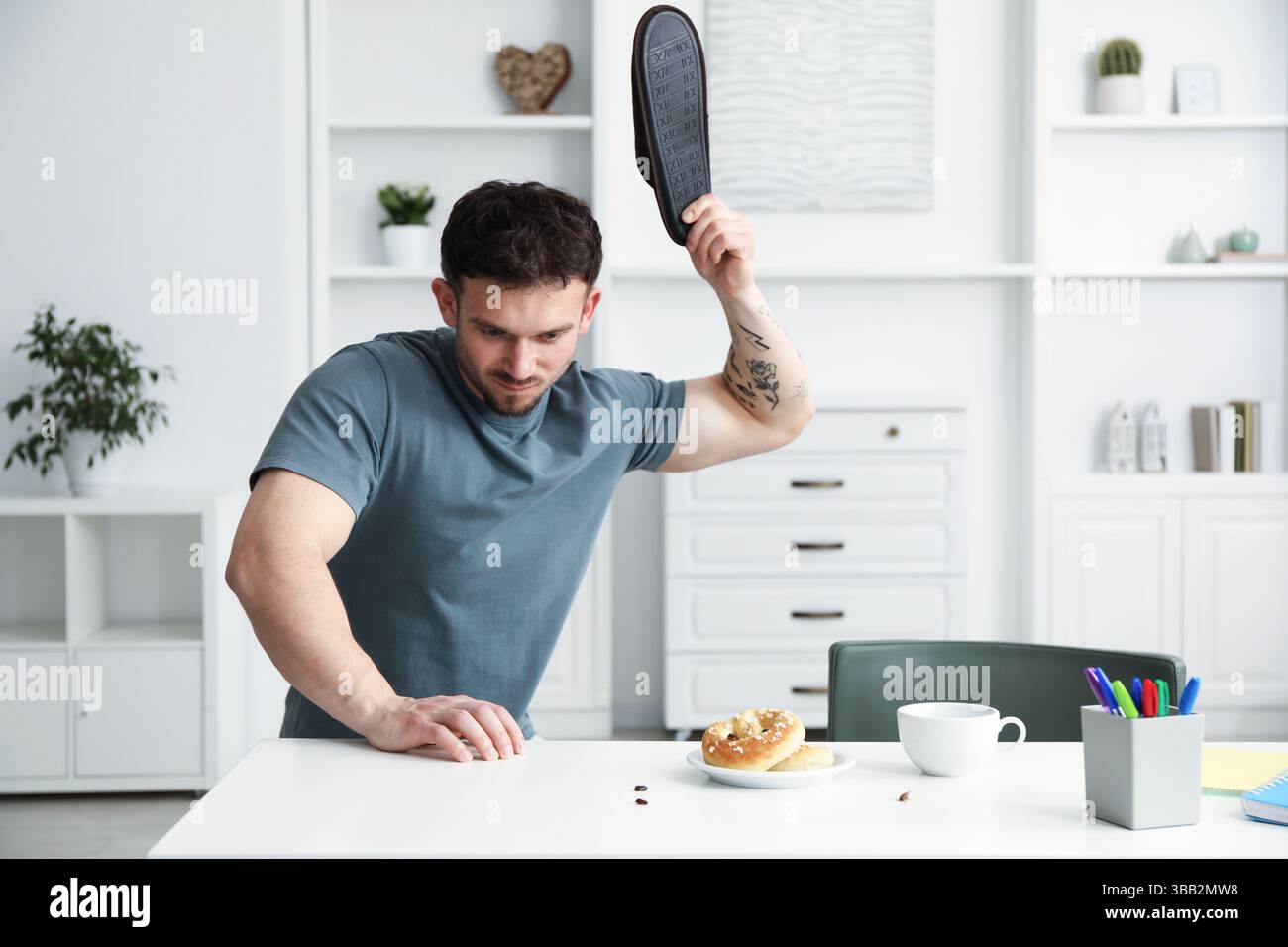 Emotional young man killing cockroaches with slipper at white table ...