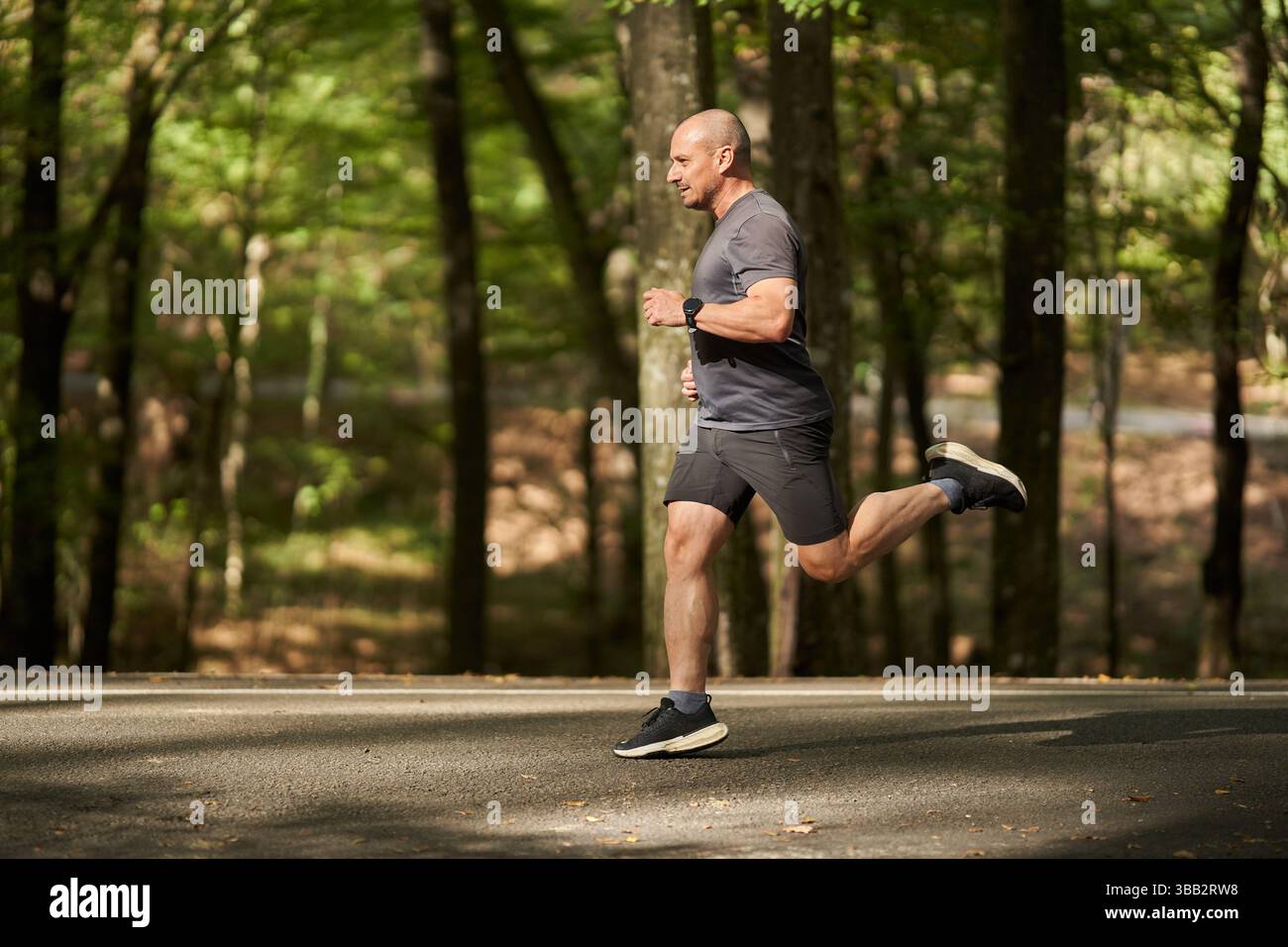 Mature man running along paved forest path during workout in natural ...