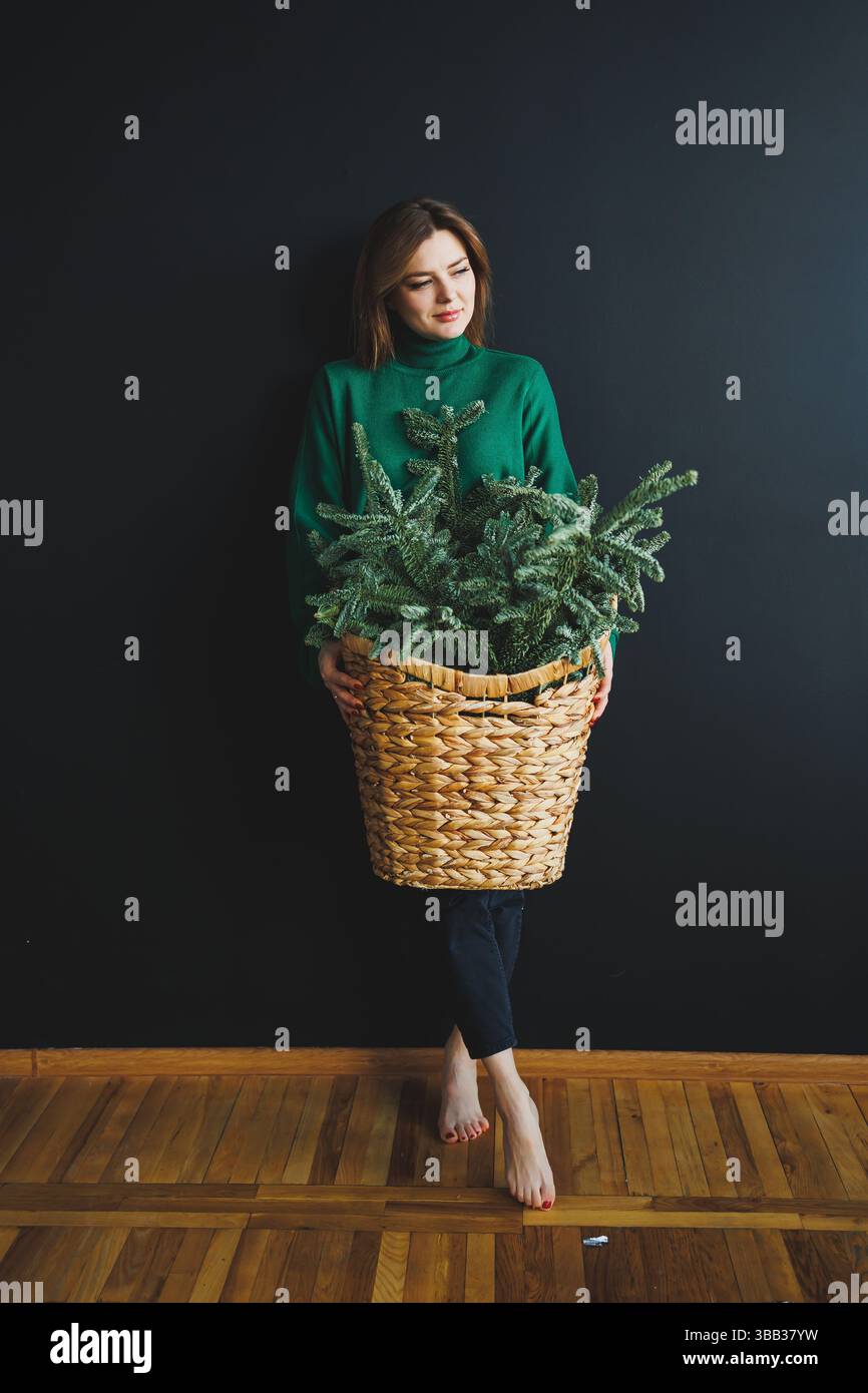 A stylish woman in a vibrant green outfit poses barefoot with a wicker ...