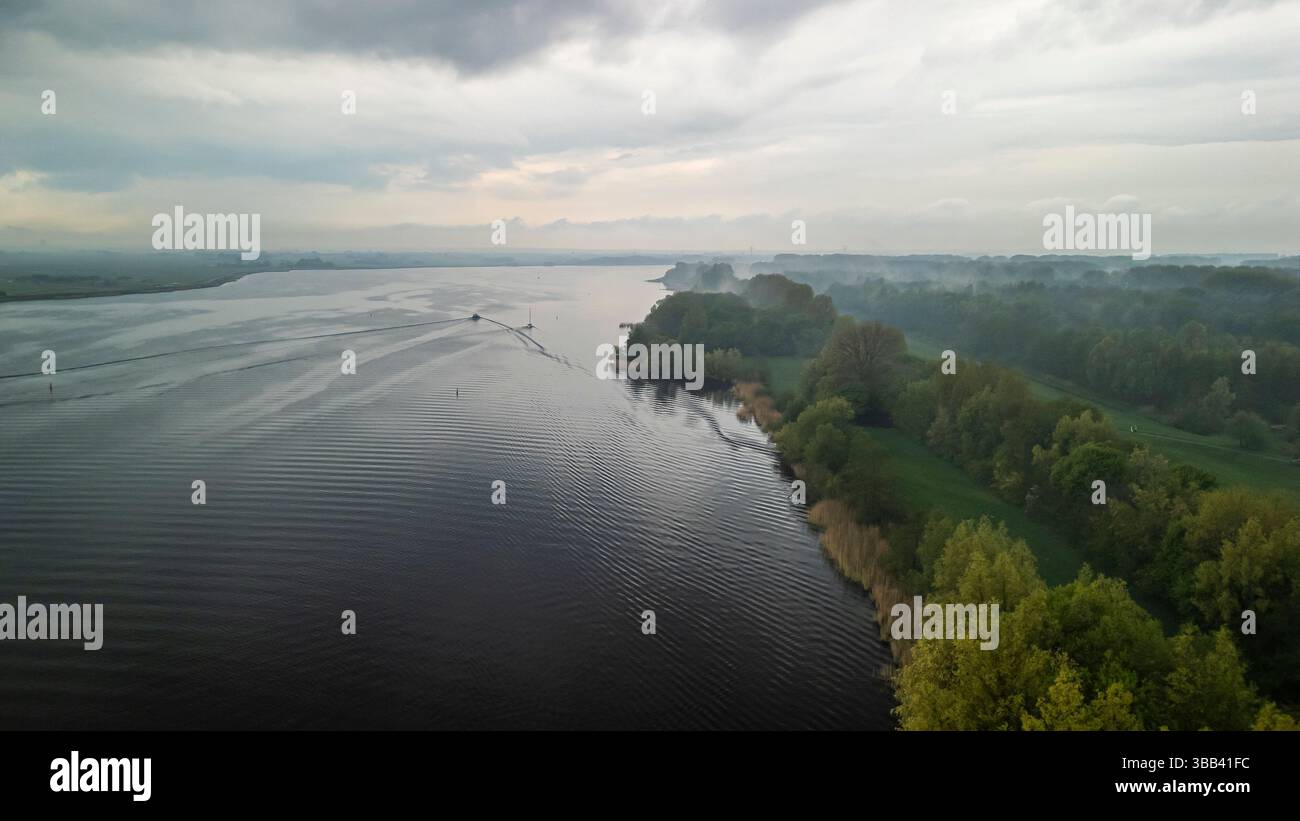 Tranquil river landscape with boat creating ripples surrounded by lush ...