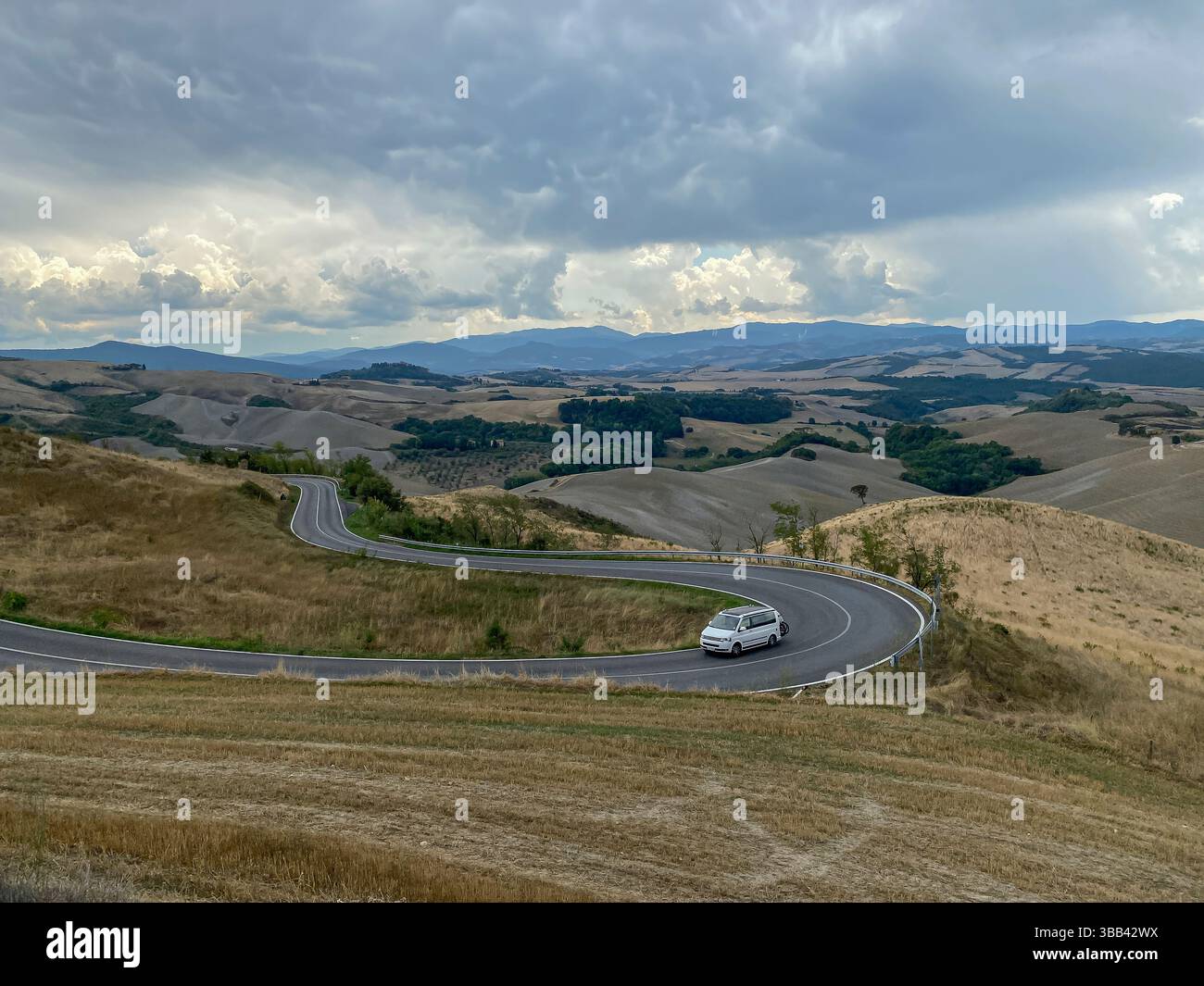 A winding countryside road curves through rolling green hills, with a ...