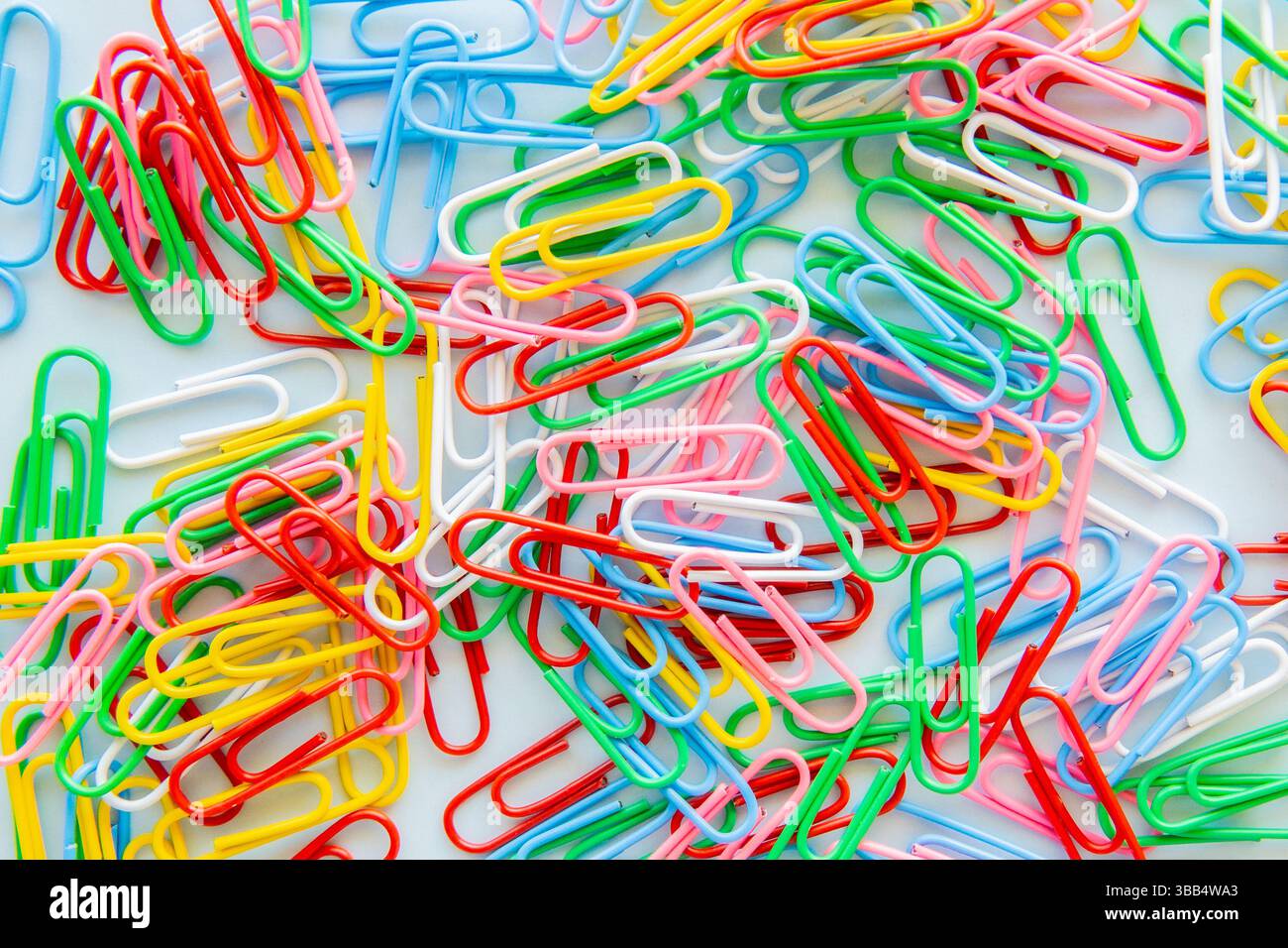 Colorful paperclips scattered across light surface represent creative ...