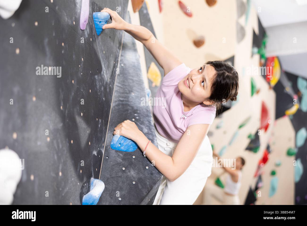 Sporty woman climbing on bouldering wall demonstrating physical strength, technical skill, and ...