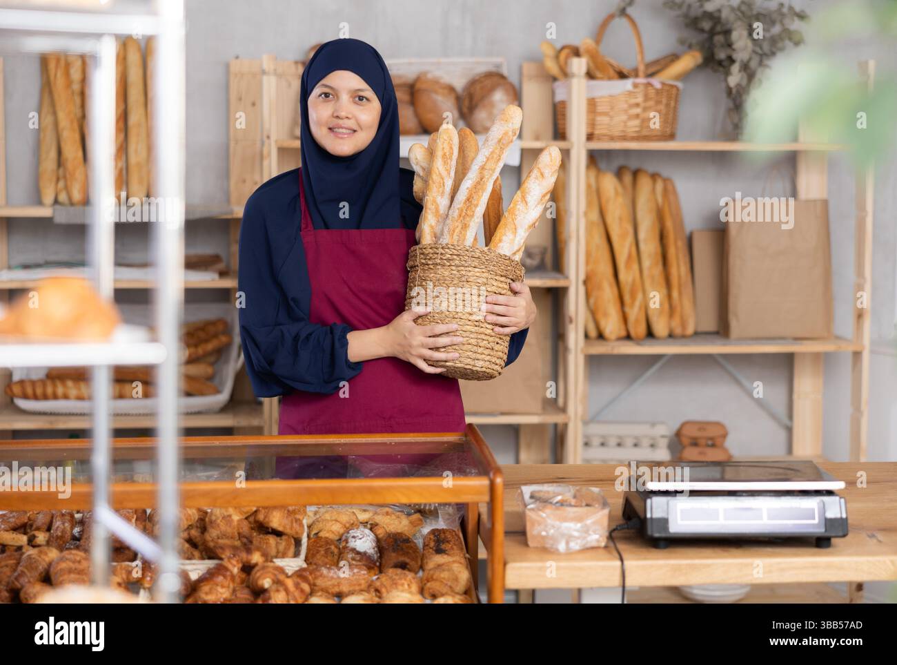 Muslim Asian woman bakery worker sells baguettes, stands at counter and ...