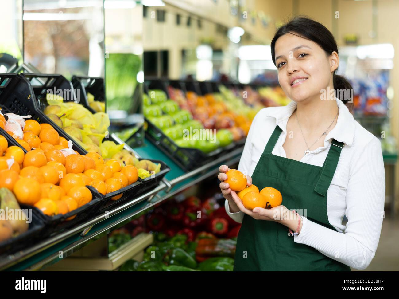 Asian female seller in apron chooses ripe mandarin Stock Photo - Alamy
