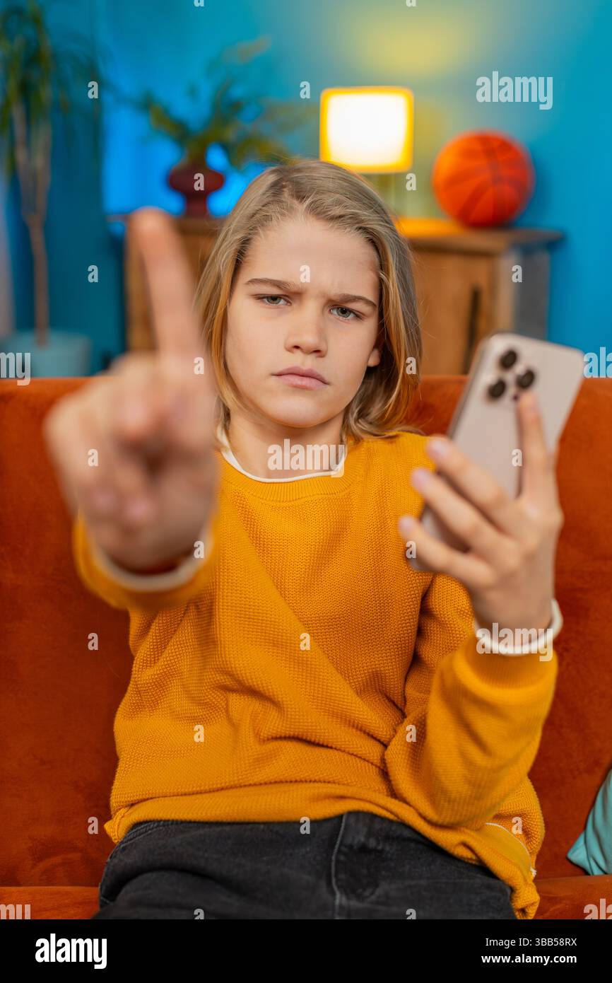 Teenager boy sits on sofa at home, waving hand in disagreement while ...