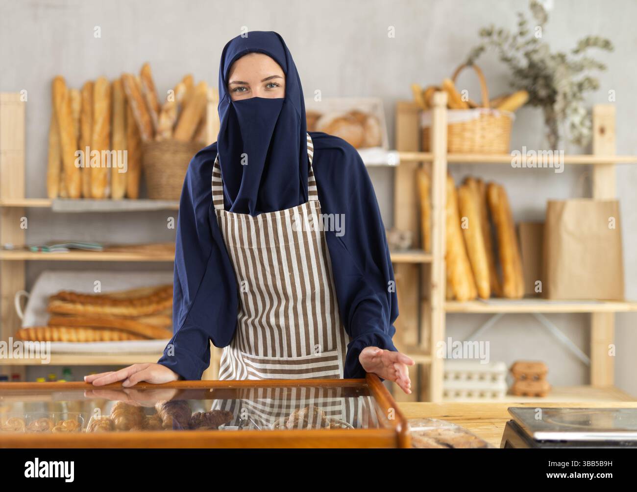 Muslim woman in apron behind pastry counter Stock Photo - Alamy