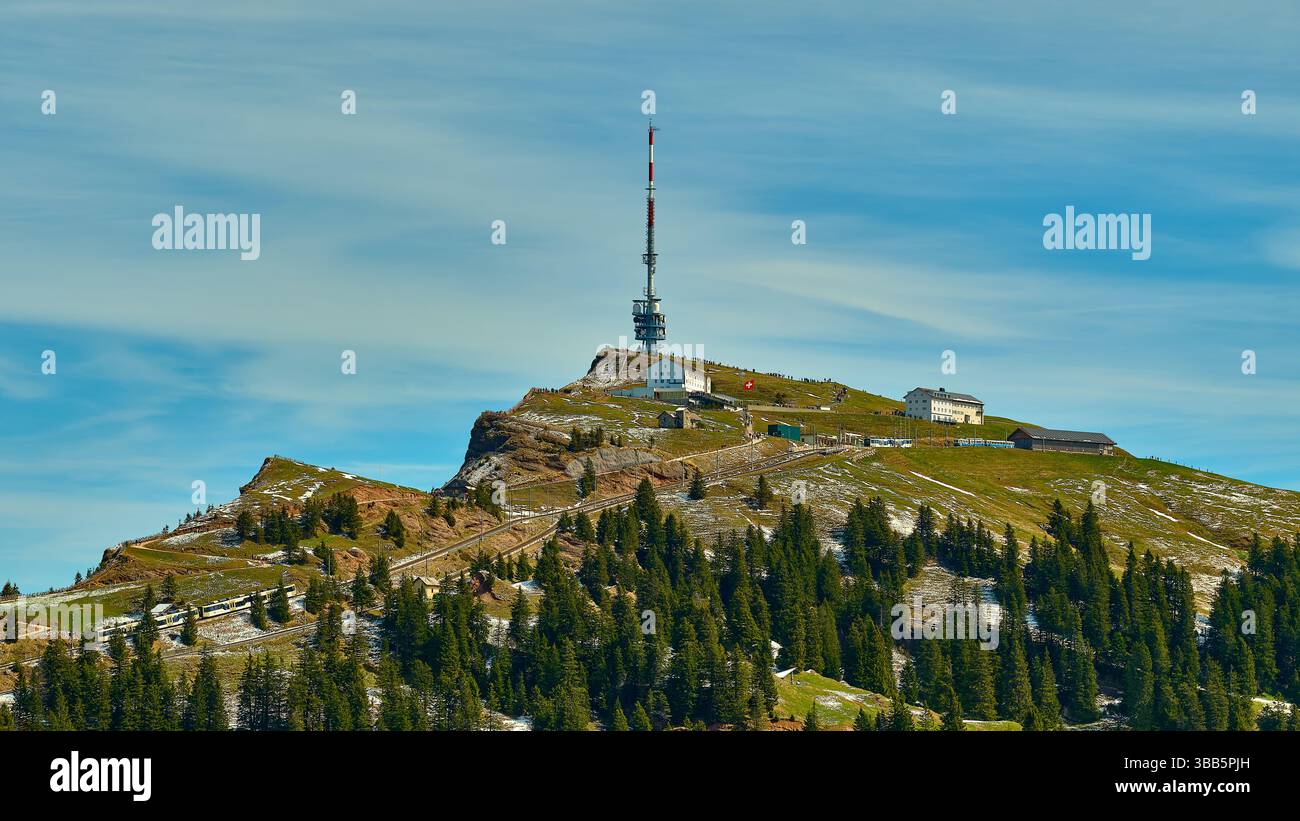 A communication tower stands tall on a mountain summit, surrounded by dense trees and rocky ...