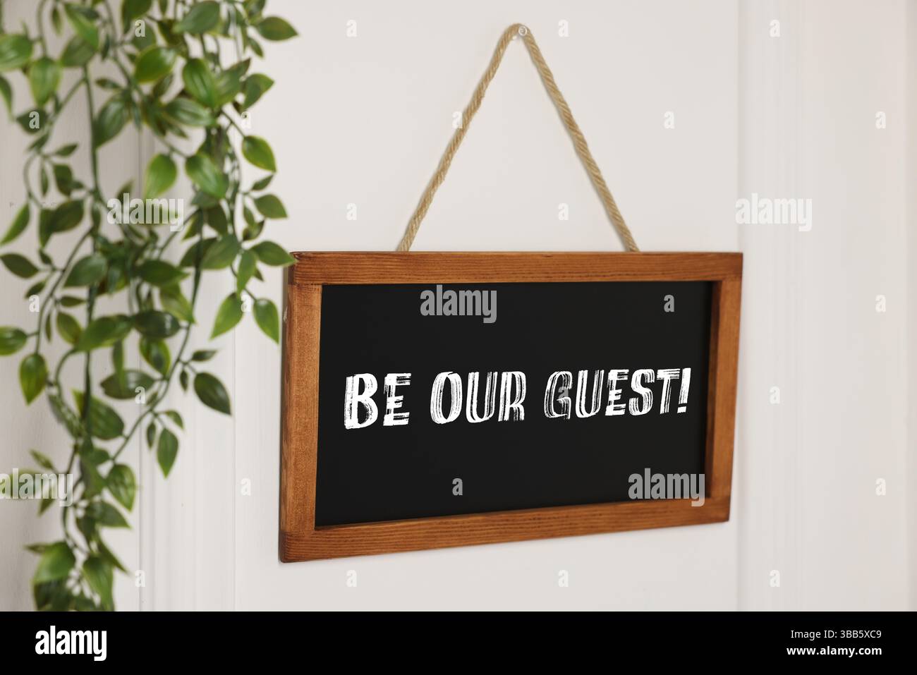 Small blackboard with phrase Be Our Guest and houseplant hanging on ...