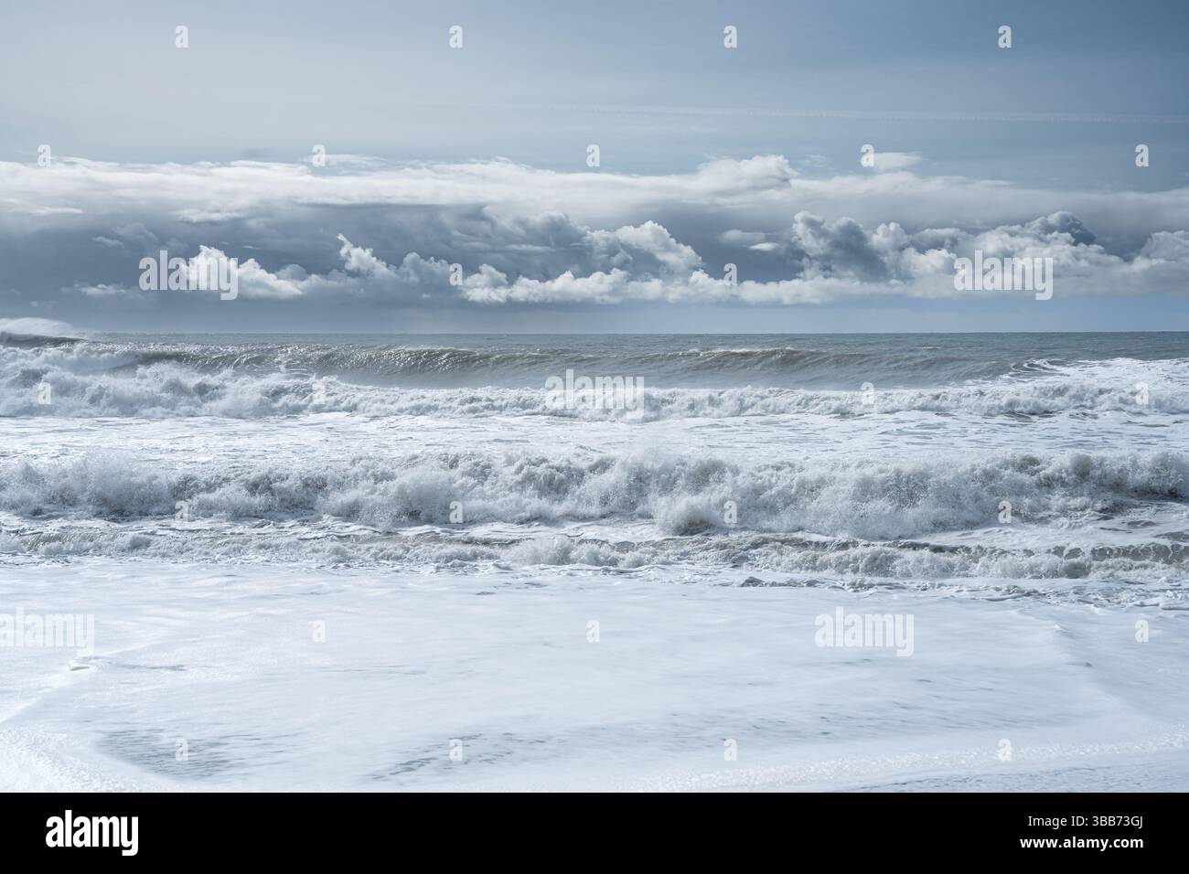 Powerful ocean waves crash along the shoreline under a dramatic cloudy ...