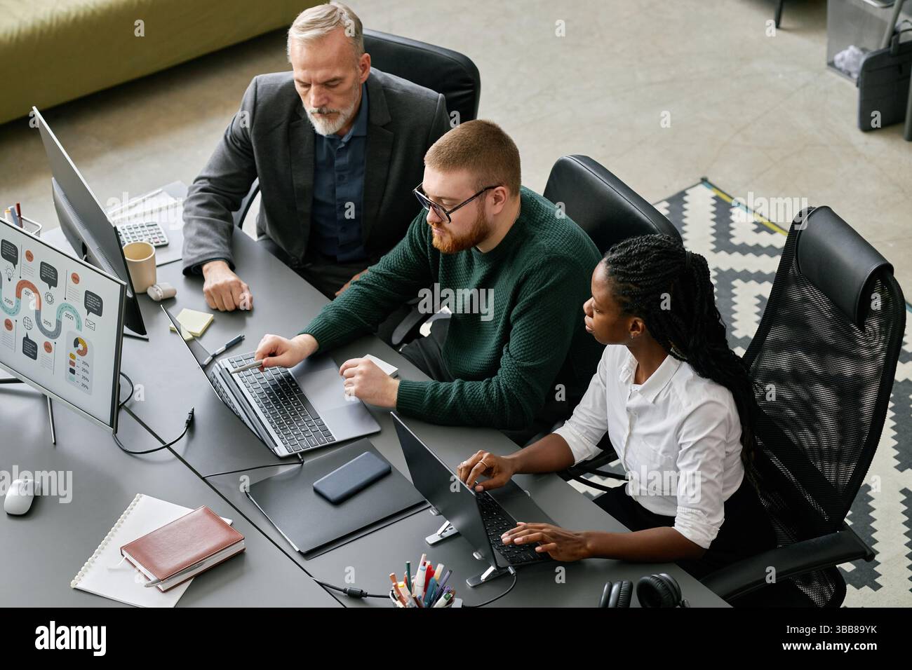 Multiracial team of three, including senior and young professionals, discussing software ...