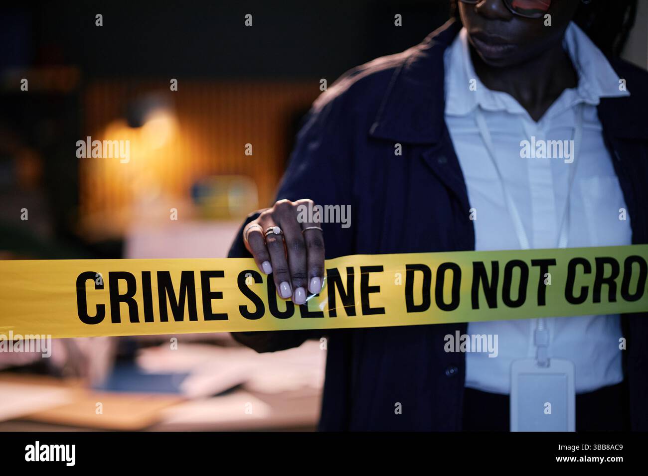 Police officer seen adjusting crime scene tape during a late-night investigation while reviewing ...