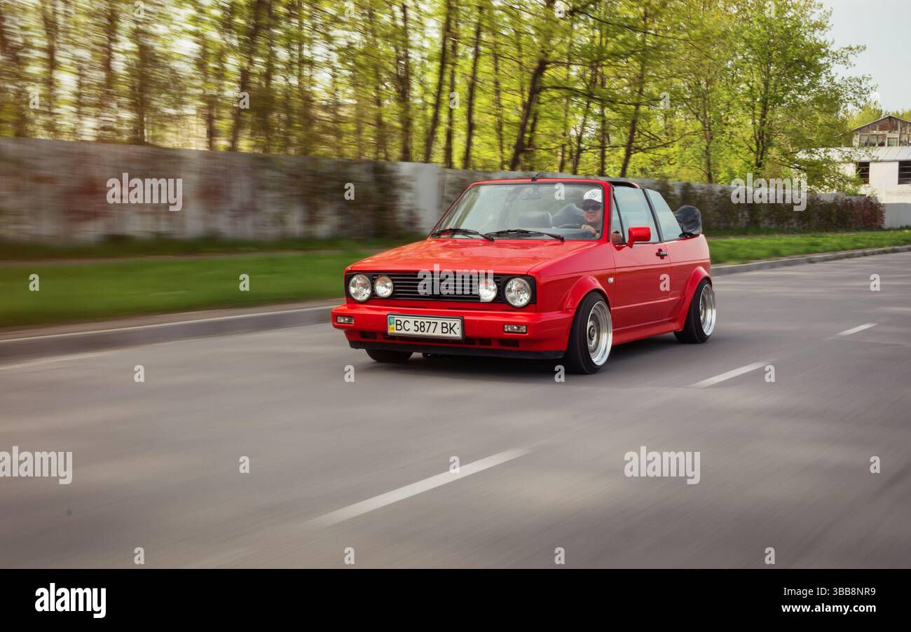 Red Volkswagen Golf mk2 cabriolet driving on a rural road. Three ...