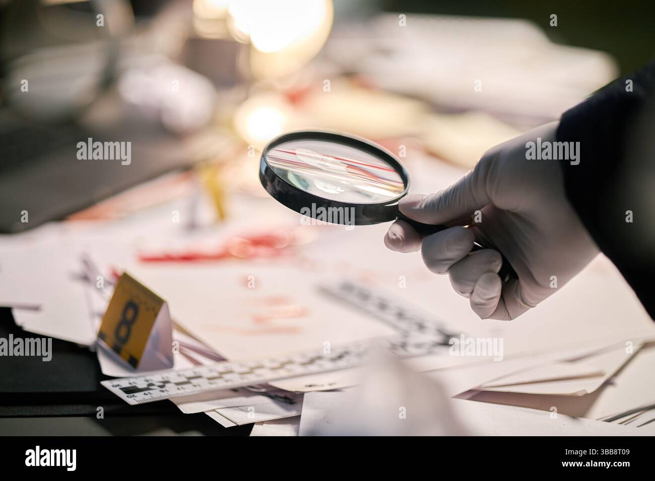 Gloved hand holding magnifying glass examining documents on cluttered ...