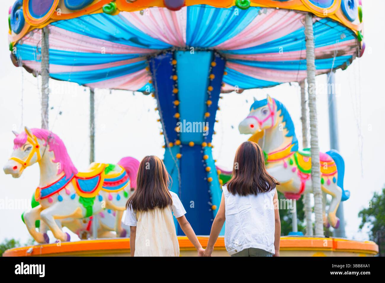 Rear view of two Asian girls having fun walking in an amusement park ...