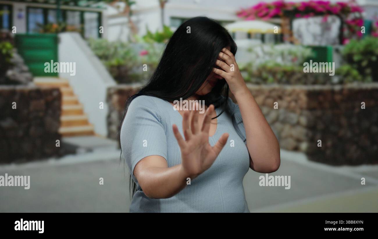 Woman covering face with hand outdoors, appearing scared, standing on ...
