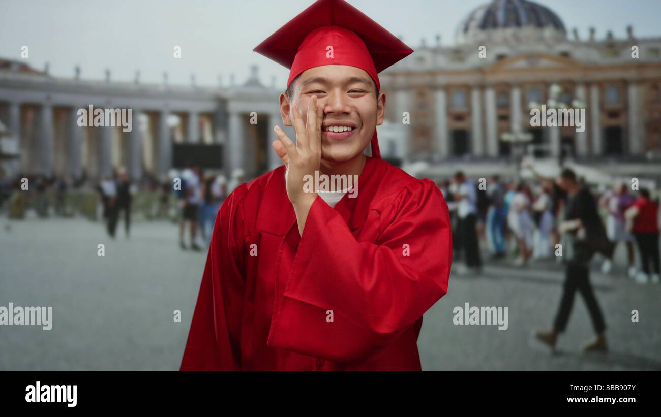 Young man in a red graduation gown joyfully gestures a secret in st ...