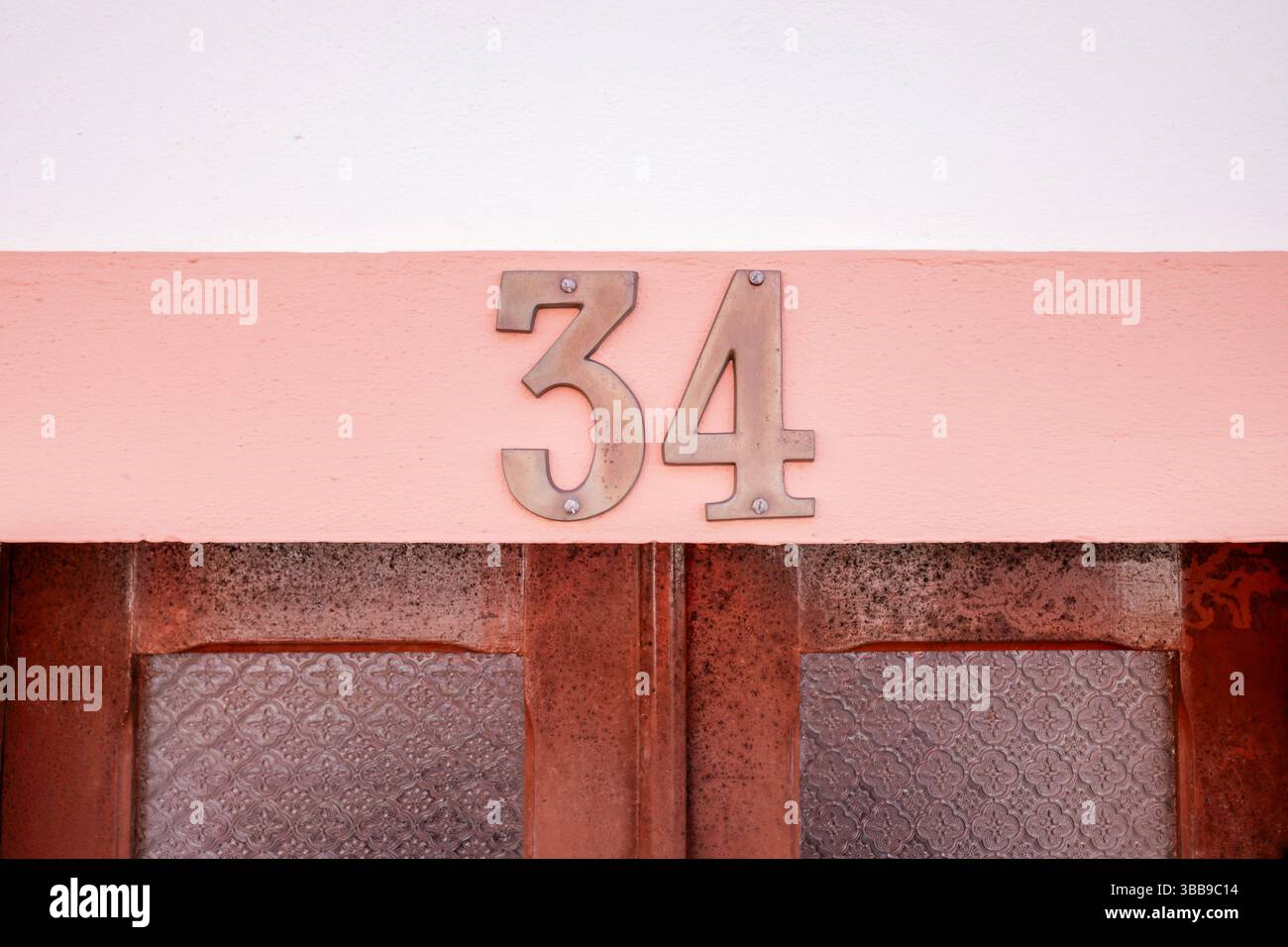 Metal House Number Thirty-Four on Peach Wall. Close-up of the metallic ...