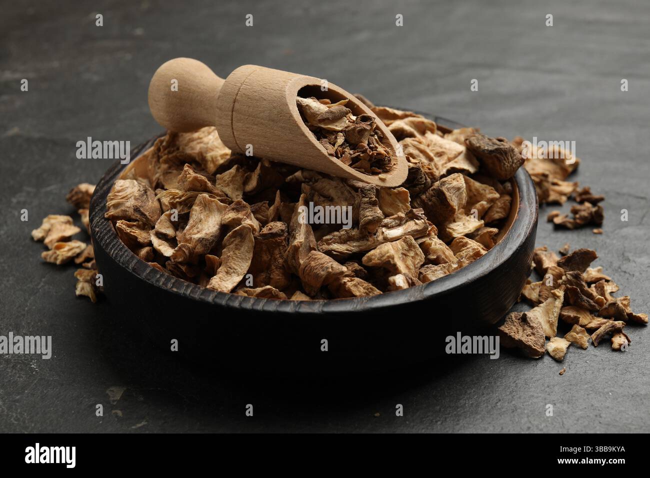 Pieces of dry chicory roots in bowl and scoop on dark textured table ...