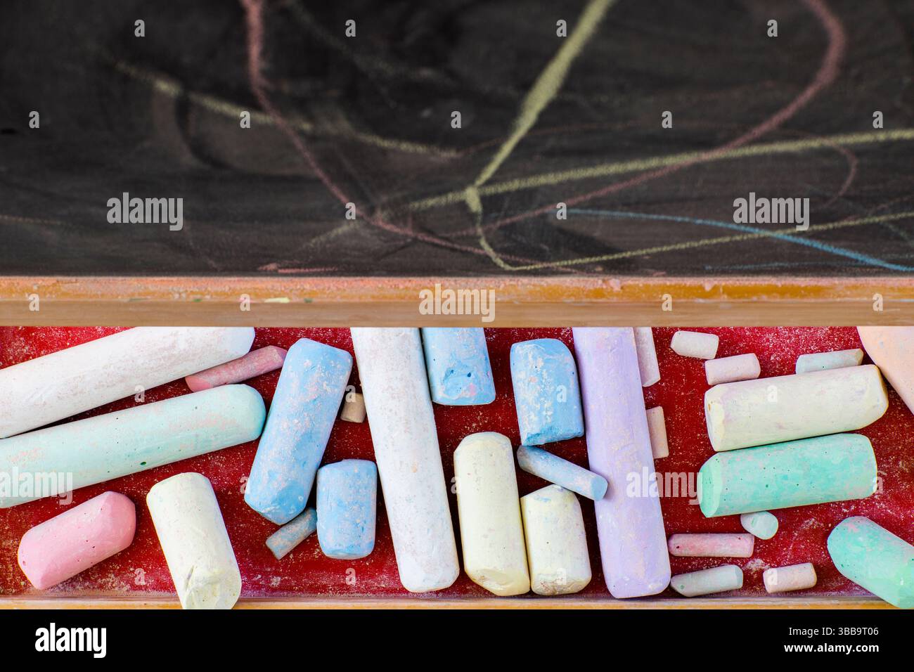 Colourful chalk pieces rest on a red tray beneath a blackboard, showing ...