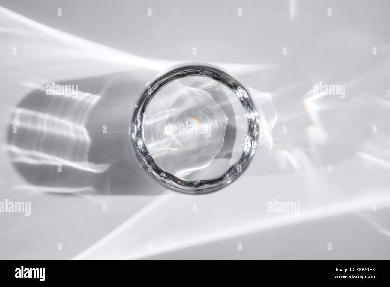 Glass of water resting on a white surface, creating an elongated and ...