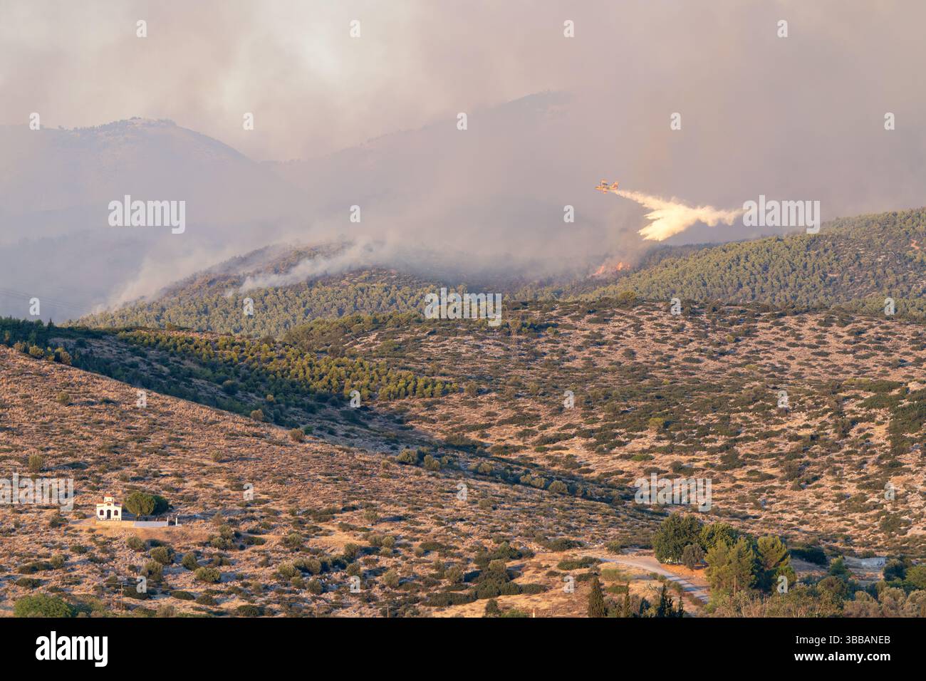 Firefighting plane drops water over forest wildfire in hilly terrain ...