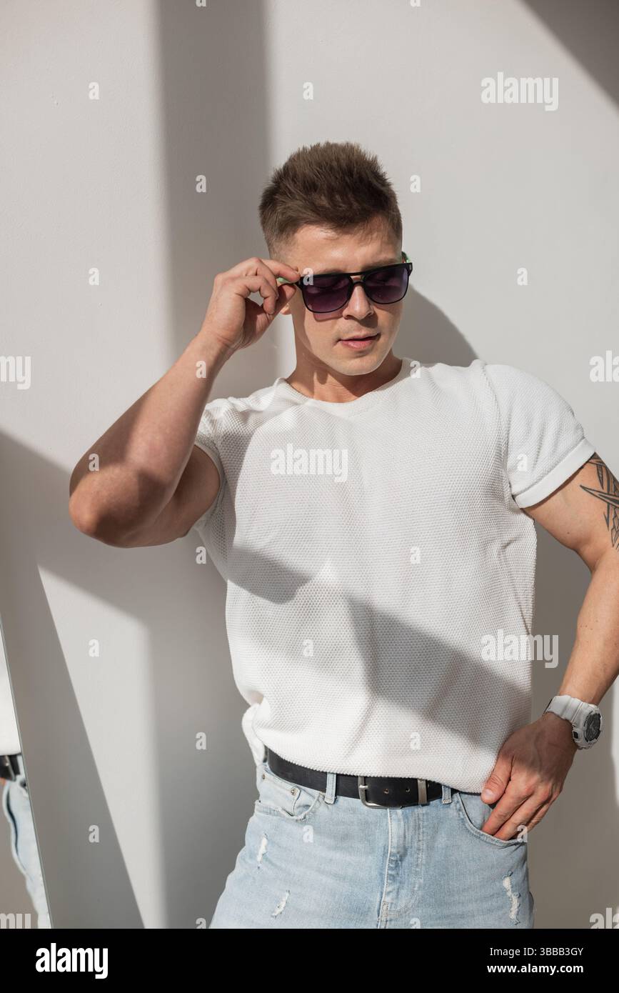 Young Male Model In White T-shirt And Ripped Jeans Poses Against A ...