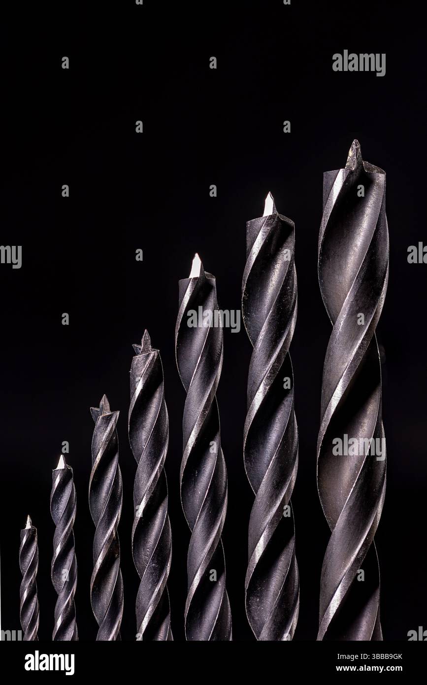 Several drill bits of increasing sizes are standing upright against a ...