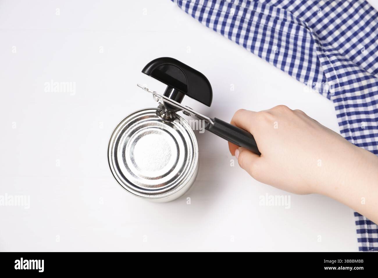 Woman opening tin with can opener at white table, top view Stock Photo ...