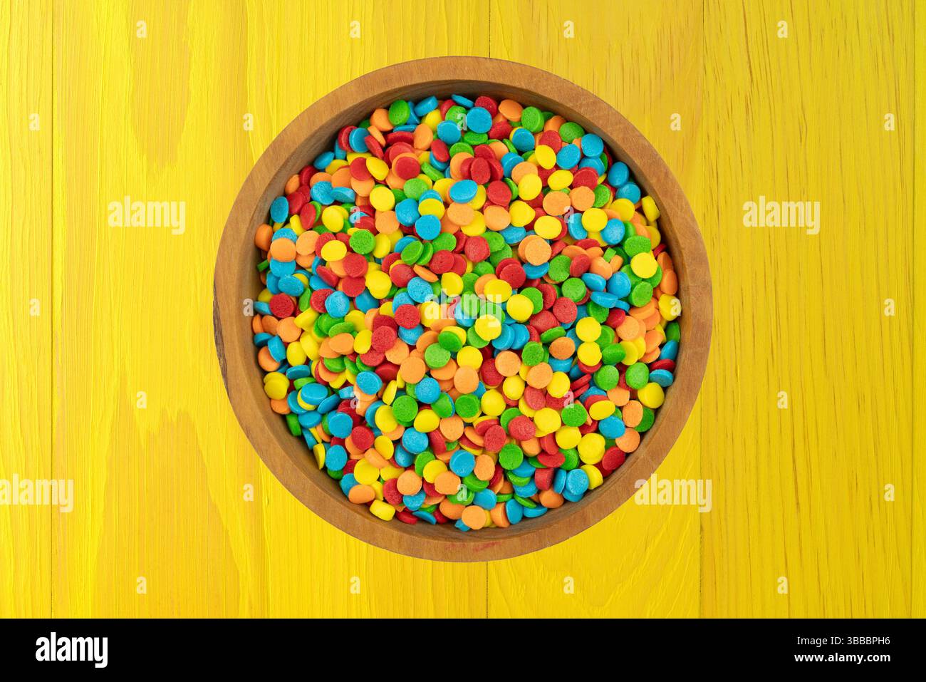 Top view of round cake sprinkles in a small wood bowl on a colorful ...