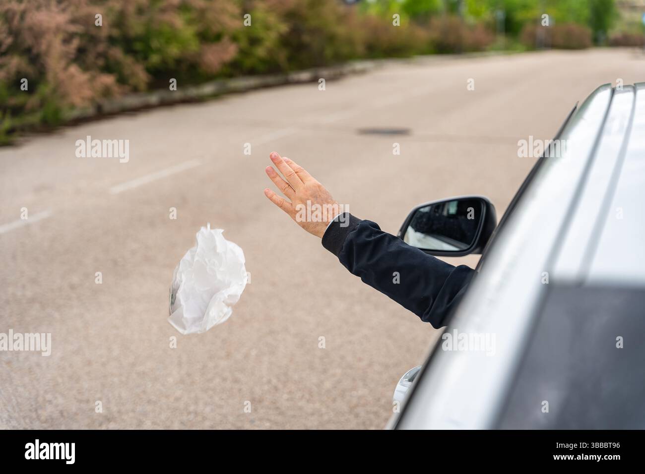A man's hand throwing garbage from the window of his car into the road ...
