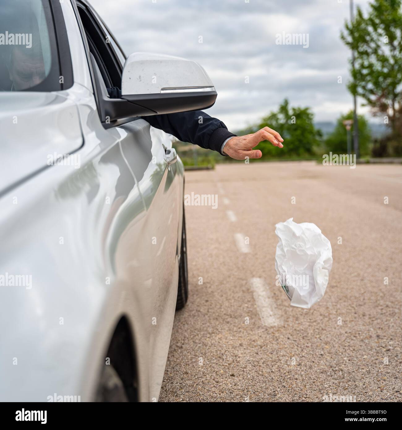 A man's hand throwing garbage from the window of his car into the road ...
